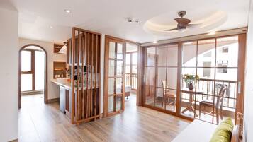Um quarto amplo com piso de madeira, área de refeições com mesa e cadeiras, e uma grande porta de vidro deslizante que dá para uma área externa.