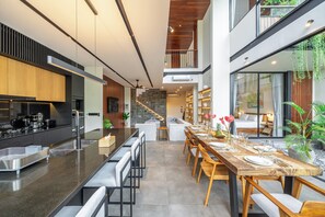 Cozinha moderna com ilha central, área de jantar com mesa de madeira comprida e escada que leva a um andar superior.