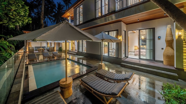 Uma casa moderna com piscina, cadeiras de sol e um grande guarda-sol.