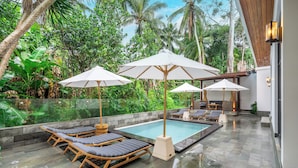 Uma área de piscina com espreguiçadeiras e guarda-sóis, rodeada por vegetação exuberante.