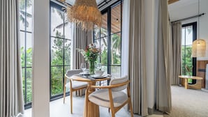 Uma área de refeições moderna com uma mesa redonda, duas cadeiras, um lustre e vista para o verde lá fora.