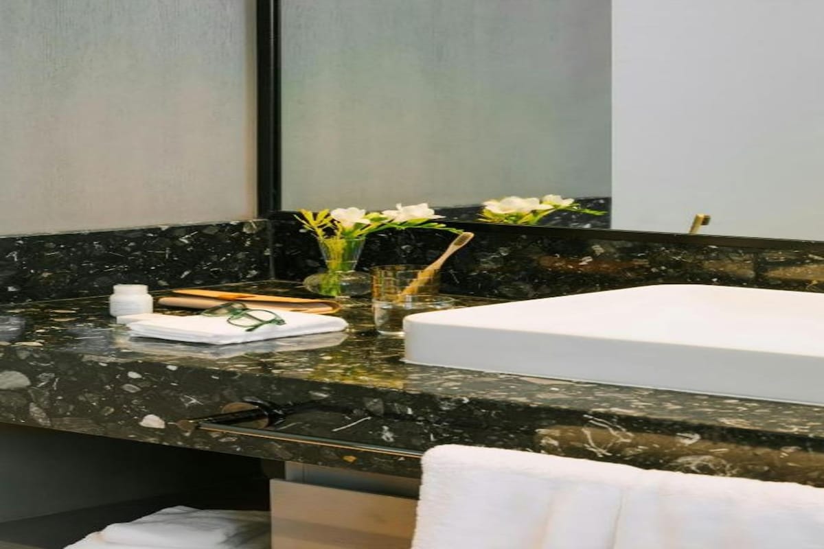 Uma casa de banho com bancada de mármore, lavatório branco e espelho.