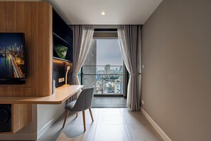 Uma sala de estar moderna com televisão, mesa de jantar, uma cadeira, varanda com cortinas e vista para a cidade.
