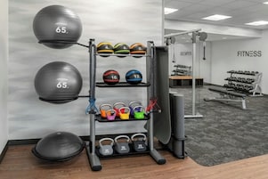 Uma academia com equipamentos de musculação, incluindo kettlebells, medicine balls e halteres.
