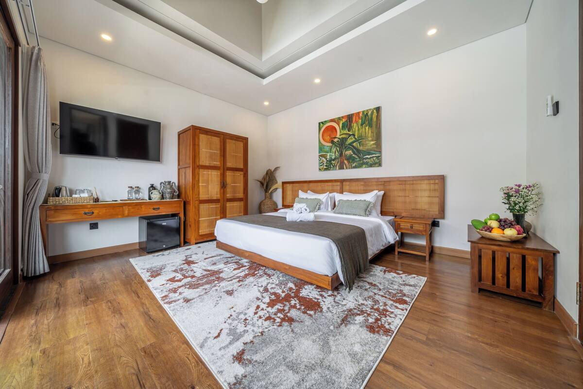 Quarto com cama, escrivaninha, televisão, obras de arte e uma fruteira.