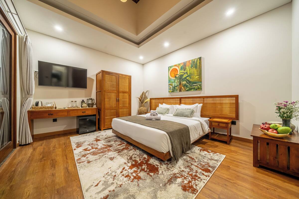 Quarto com cama, mobiliário de madeira, televisão e pintura.