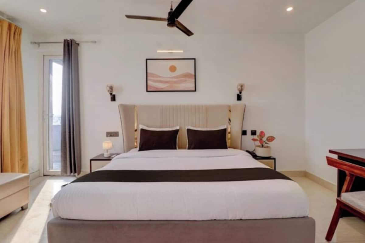 Quarto com cama, ventilador de teto, mesa de cabeceira, abajur, um quadro na parede e vista para o exterior.