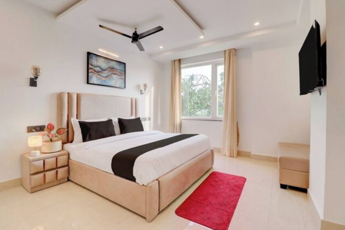Quarto moderno com cama, mesa de cabeceira, luminária, obra de arte, ventilador de teto e janela com cortinas.