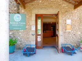 Entrada de um edifício de pedra com uma placa indicando 'Terres de France Domaine des Vans' e duas pequenas carroças do lado de fora.