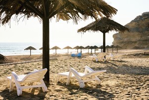 Uma praia com espreguiçadeiras brancas e guarda-sóis de palha.