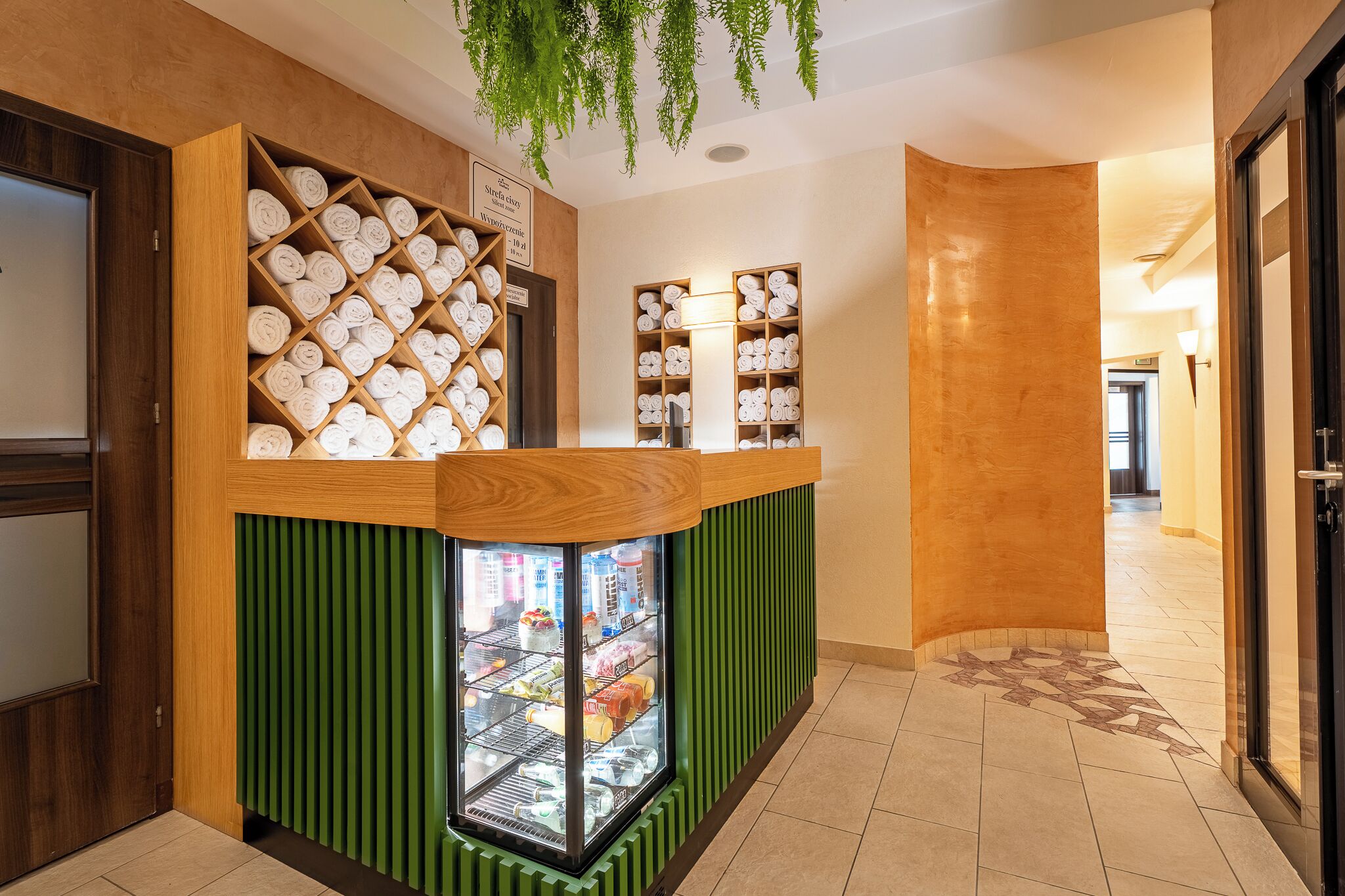 Uma área de recepção com balcão de madeira, vitrine de vidro e painel verde.