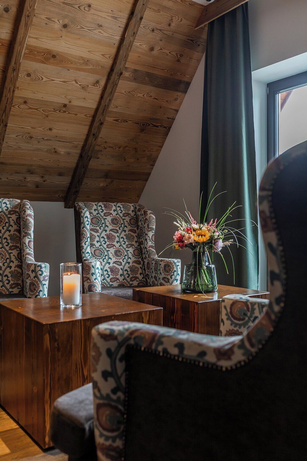 Uma área de estar acolhedora com cadeiras estampadas, uma mesa, uma vela e um vaso com flores.