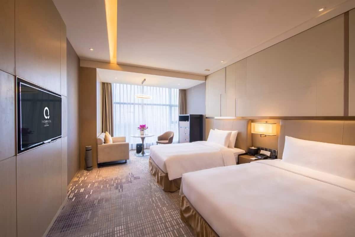 Quarto de hotel com duas camas, televisão, escrivaninha e janela com cortinas.