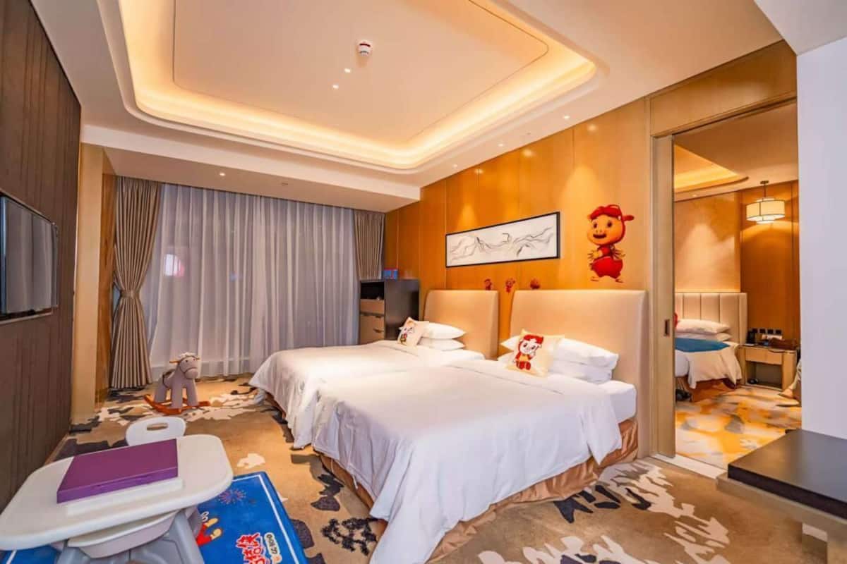 Quarto de hotel com duas camas, televisão, escrivaninha e banheiro visível por uma porta aberta.