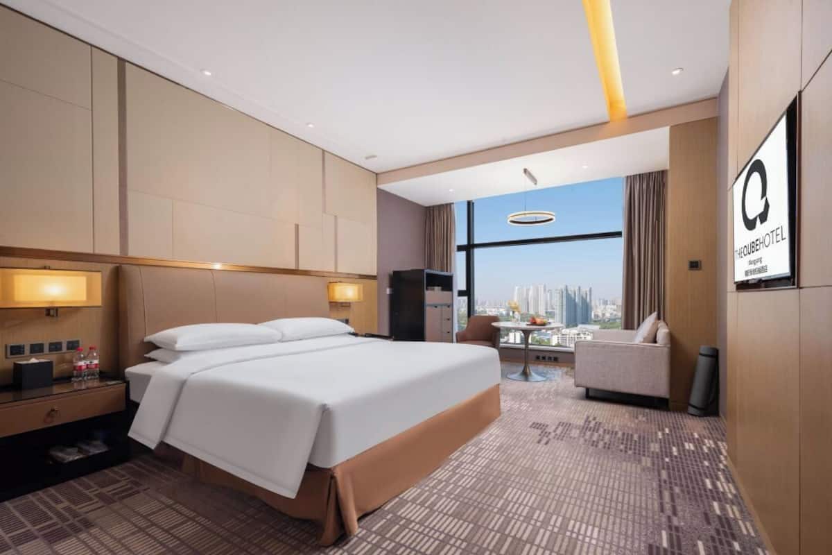 Quarto de hotel com uma cama grande, escrivaninha, cadeira, televisão e vista para a cidade.