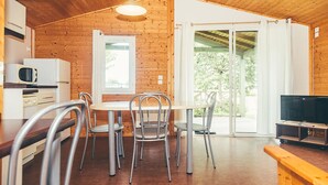 Interior em madeira com mesa de jantar, cadeiras, televisão e porta de vidro deslizante para o exterior.