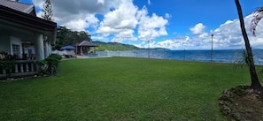 Uma área gramada com vista para o mar, um edifício com varanda e um coreto.