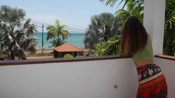 Uma varanda com vista para o mar, palmeiras e um pequeno edifício.