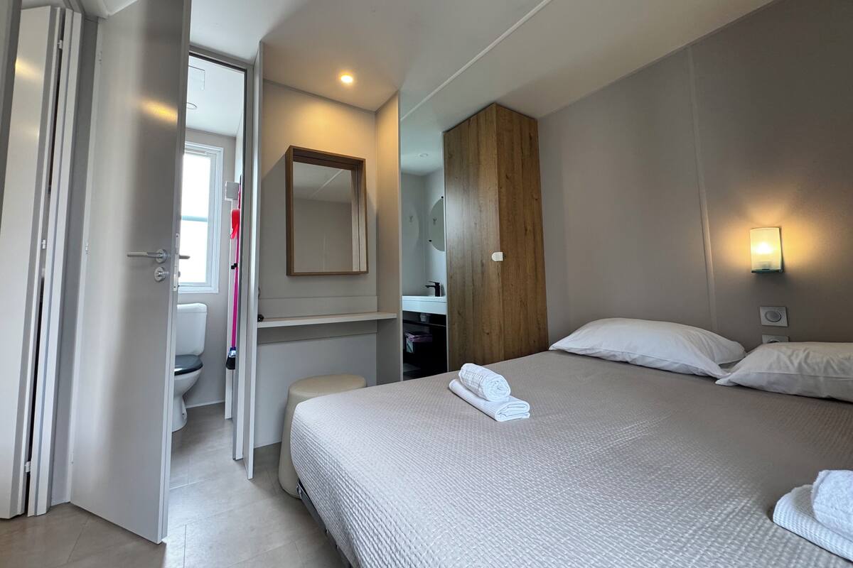 Quarto de hotel com uma cama, um guarda-roupa de madeira, uma casa de banho com sanita e lavatório, e um espelho na parede.