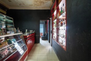 Um corredor estreito, com uma vitrine de vidro à esquerda, um balcão com superfície vermelha e prateleiras com garrafas à direita.