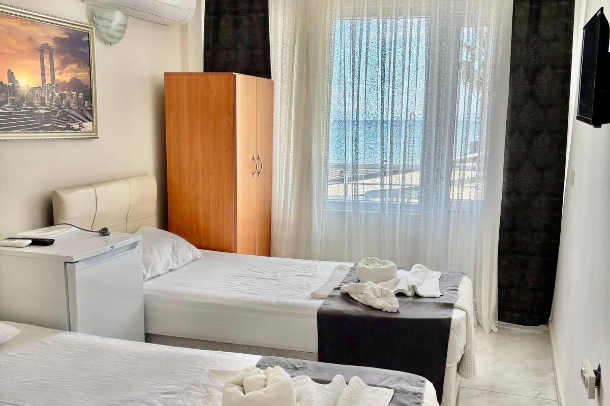 Quarto de hotel com duas camas, guarda-roupa, secretária, cadeira, aquecedor, janela com cortinas e ar condicionado fixado na parede.