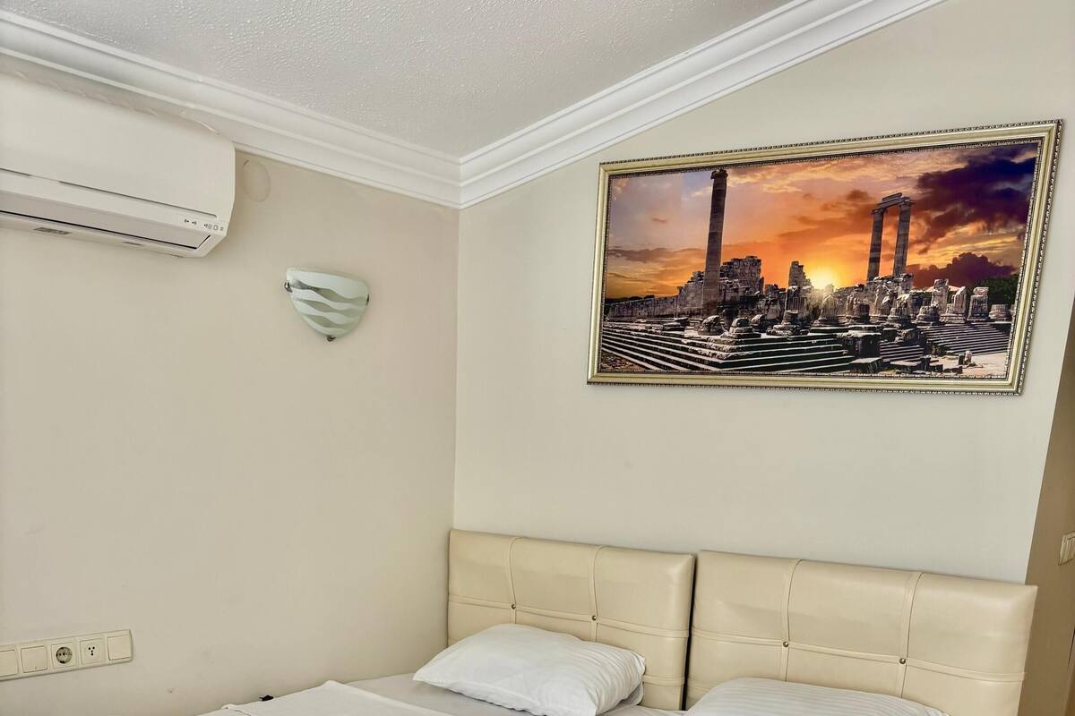 Quarto de hotel com uma cama, um quadro de uma paisagem urbana e um aparelho de ar condicionado branco.