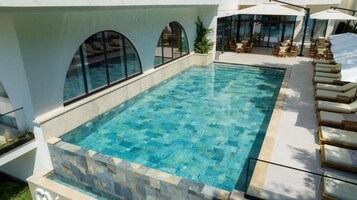 Piscina retangular com água cristalina, rodeada por uma área de lazer com espreguiçadeiras e guarda-sóis.