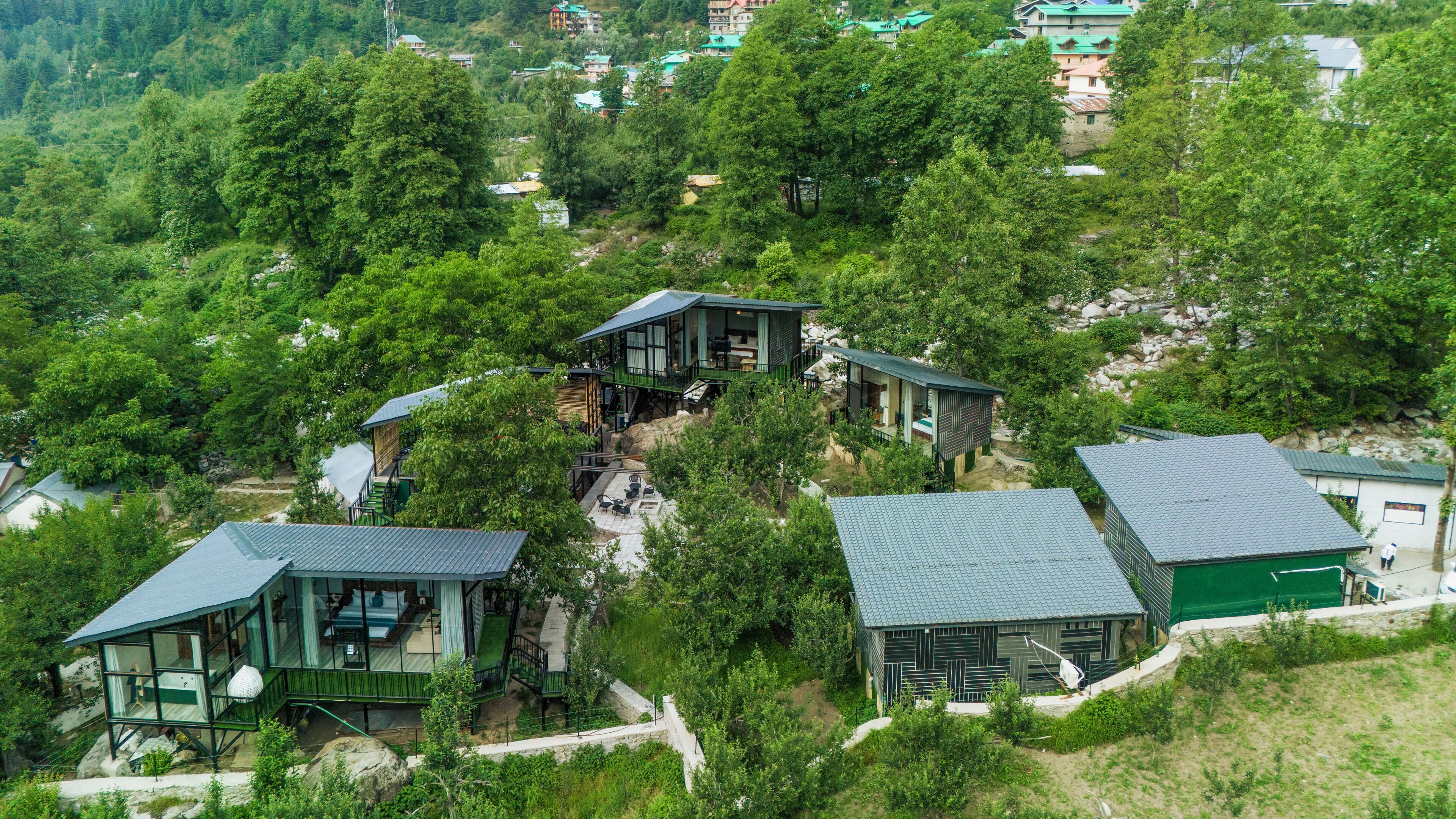 Um conjunto de cabanas modernas com paredes de vidro, rodeadas por uma floresta densa, e ligadas por um caminho estreito.