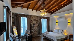Quarto com teto de madeira, duas camas, parede de pedra, uma mesa e uma cadeira.