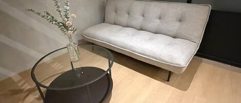 Quarto moderno com sofá cinzento, mesa de vidro com base preta e um vaso com flores.