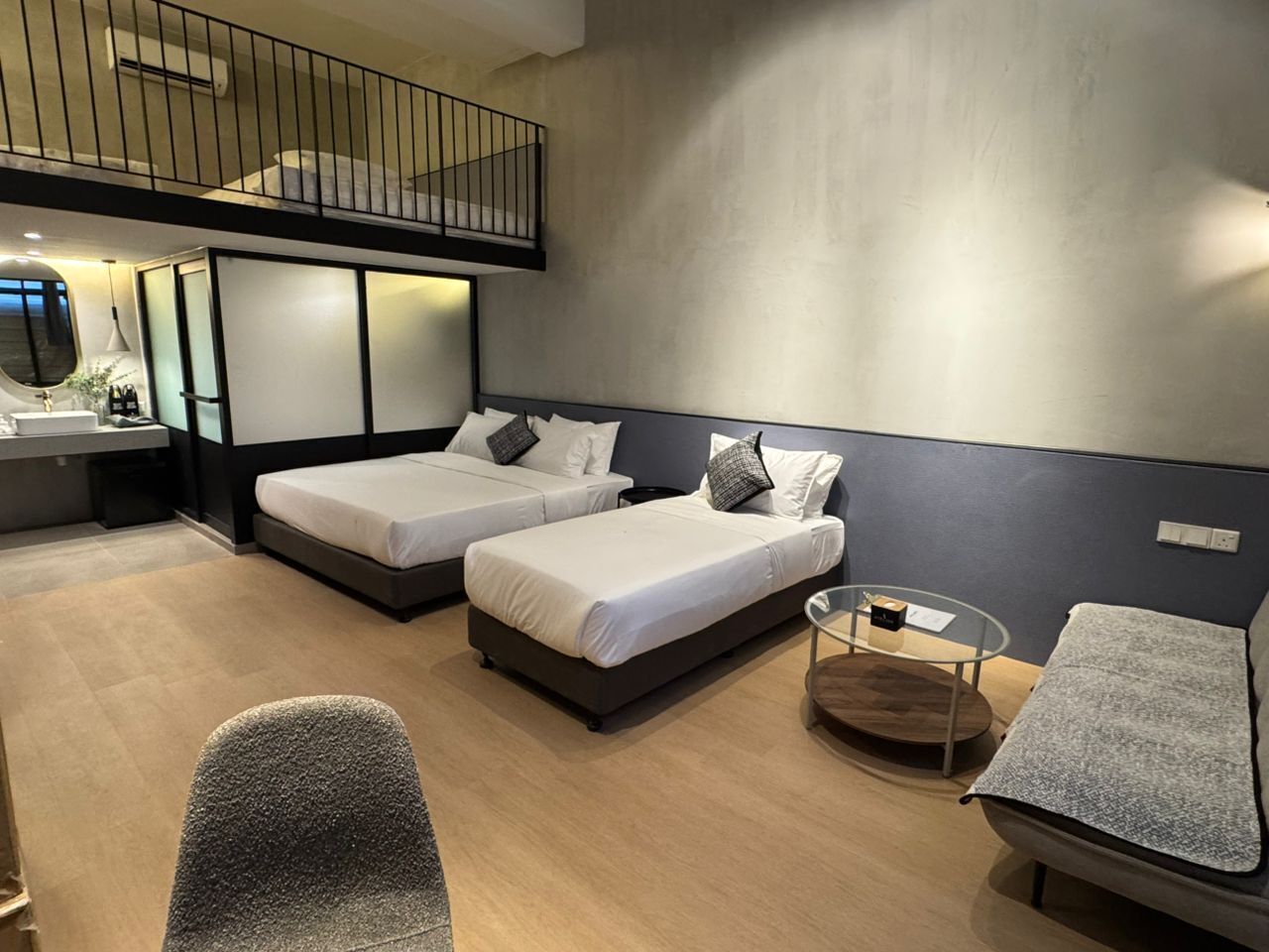 Quarto moderno com duas camas, uma mesinha, uma cadeira e varanda.