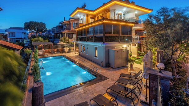 Uma casa de dois andares com piscina, área de estar ao ar livre e uma varanda bem iluminada.
