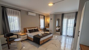 Quarto de hotel moderno com uma cama grande, uma mesinha de cabeceira, uma cadeira, uma pequena mesa redonda e um espelho.