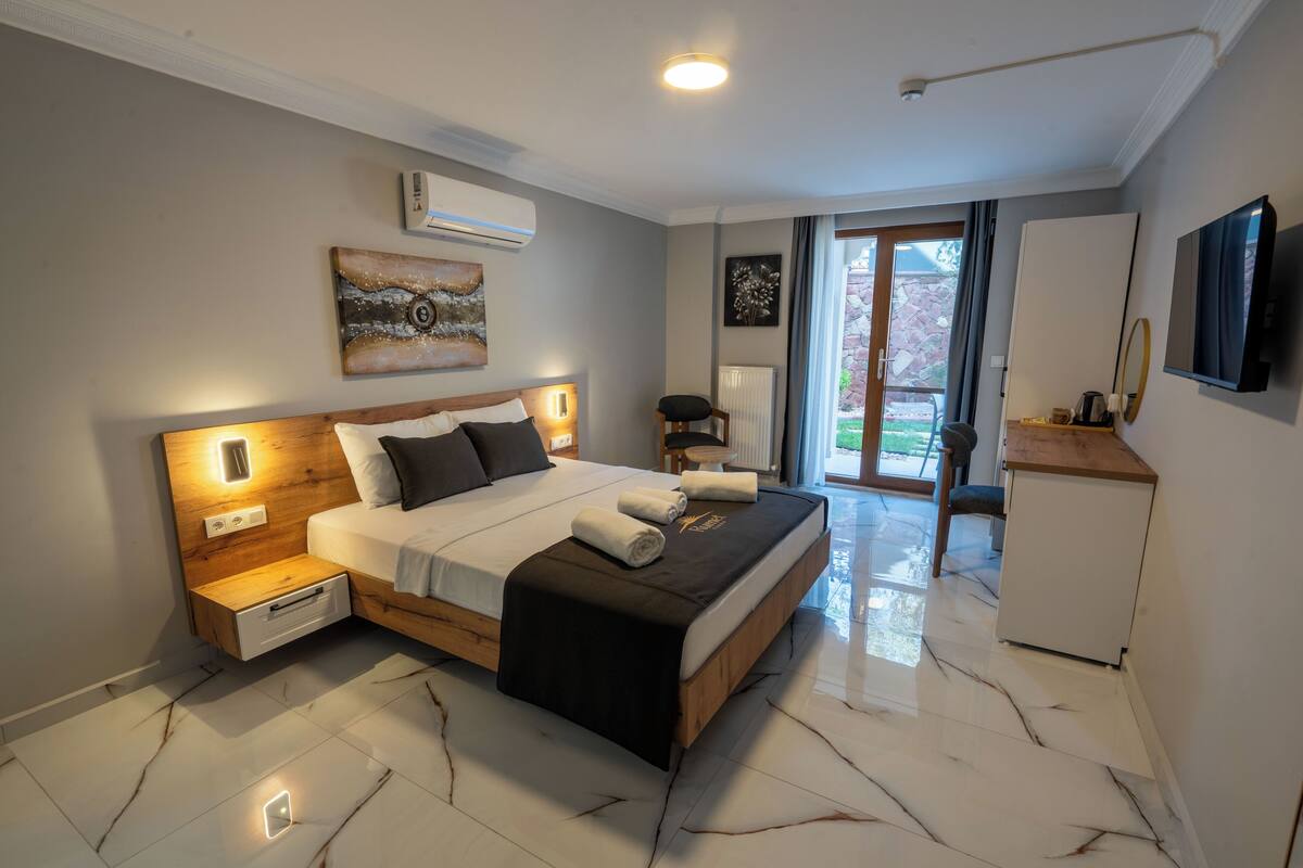 Quarto moderno com uma cama grande, mesas de cabeceira, televisão integrada e vista através de uma porta de vidro.