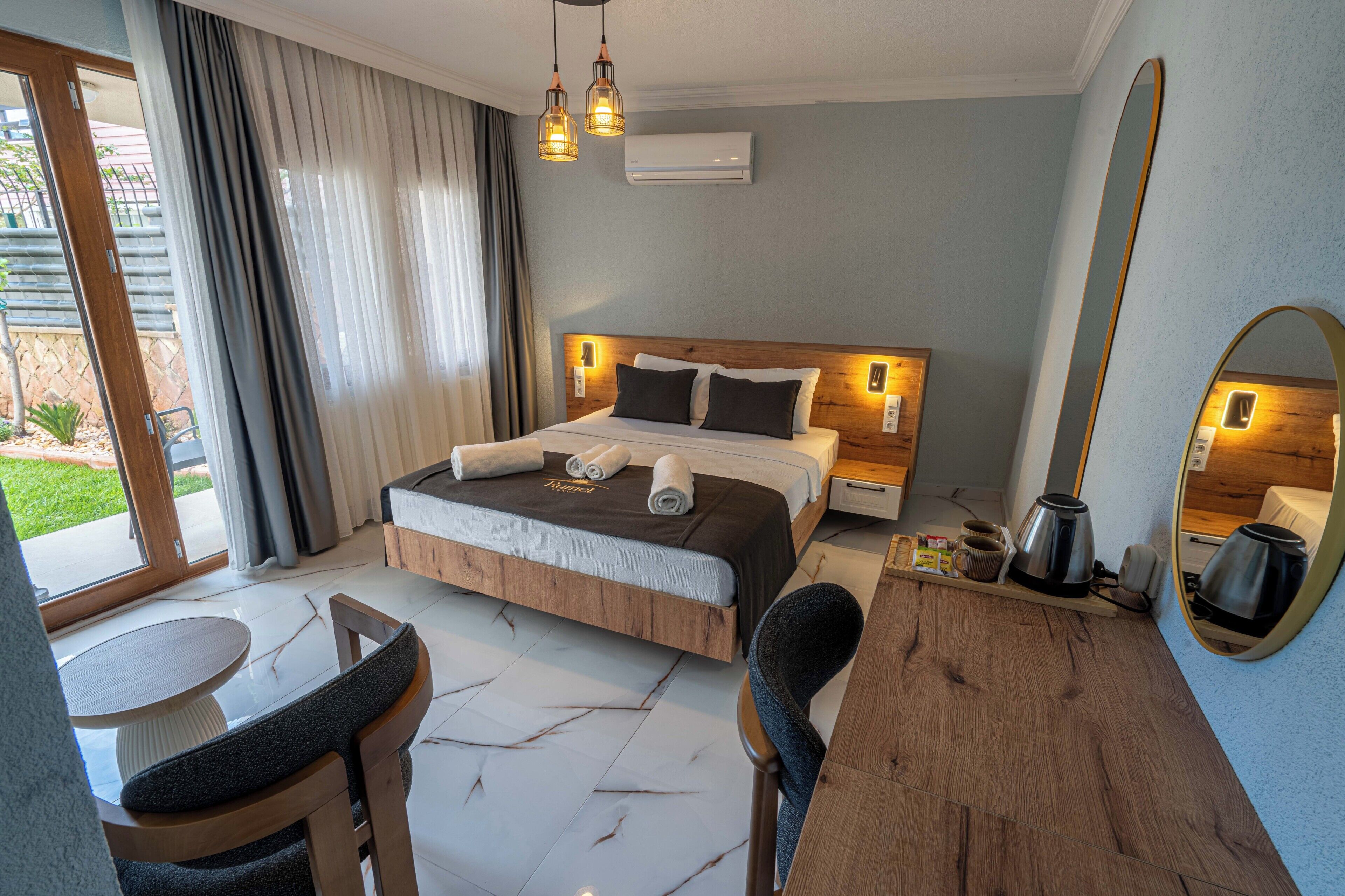 Quarto de hotel com cama, escrivaninha, cadeira, mesa redonda e um espelho grande.