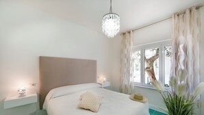 Quarto com cama, mesas de cabeceira, um candelabro, janela com cortinas e um vaso de planta.