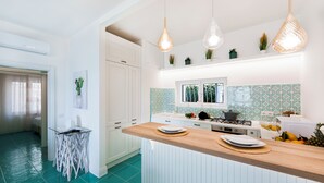 Uma cozinha moderna com armários brancos, bancada de madeira, luminárias pendentes e painel de azulejos.
