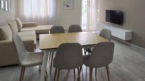 Uma sala de estar moderna com sofá, mesa de jantar, cadeiras, televisão e luminária de teto.