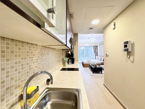 Uma cozinha moderna com pia, bancada e uma pequena planta. Há uma área de refeições com um sofá e uma mesa.