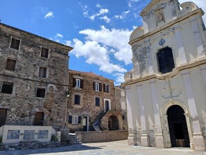Um edifício histórico com uma torre de relógio, paredes de pedra e uma escadaria que leva a um andar superior.