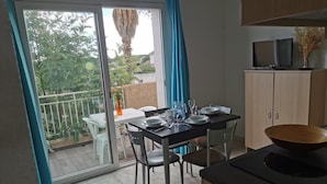 Uma sala de jantar com uma mesa posta para quatro pessoas, uma televisão em um móvel e vista para o exterior por uma porta deslizante.