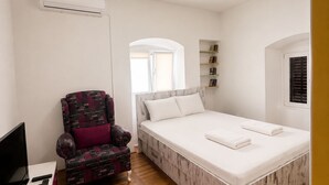 Quarto com cama, cadeira, televisão e ar condicionado.