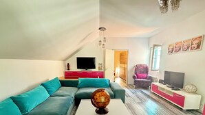 Uma sala de estar moderna com sofá seccional, mesa de centro branca, um globo, televisão e poltrona rosa.