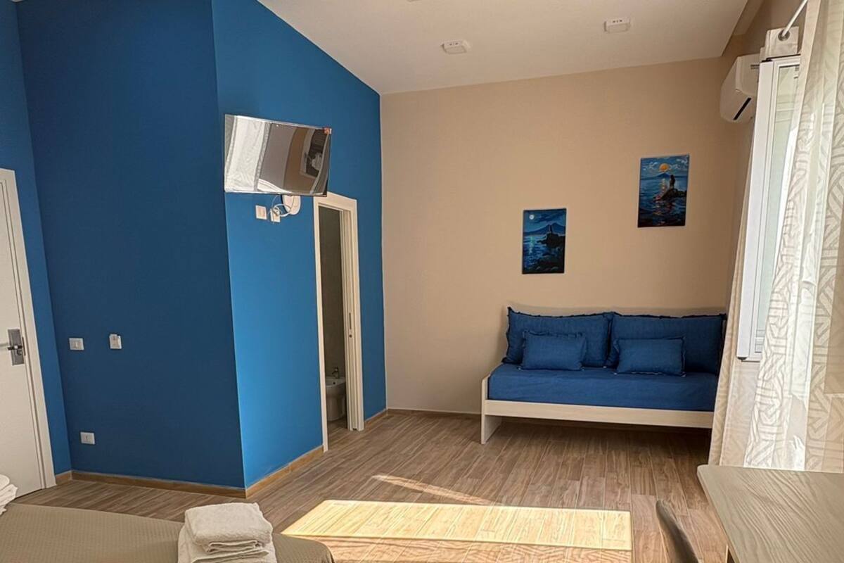 Quarto com cama, escrivaninha, sofá e banheiro.