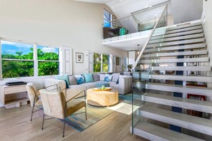 Uma sala de estar moderna com escada de vidro, um conjunto de sofá e uma área de jantar.