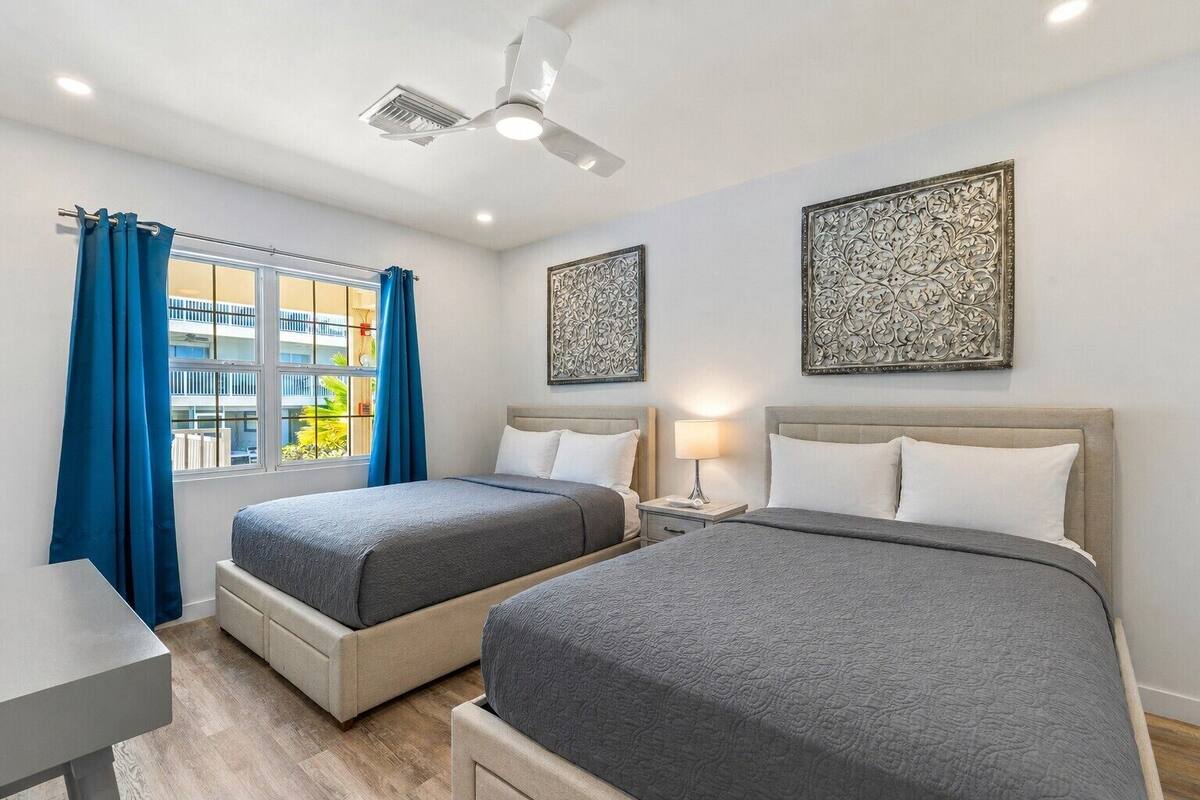 Quarto de hotel com duas camas, uma escrivaninha, ventoinha no teto e obras de arte nas paredes.