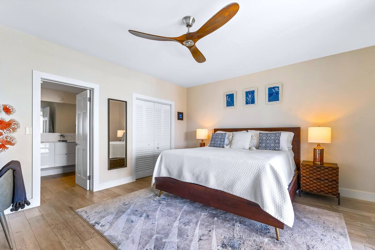Quarto com cama, ventilador de teto, abajures e mesa de cabeceira.
