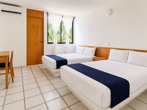 Quarto de hotel com duas camas, uma cabeceira de madeira, uma escrivaninha e uma janela com cortinas.