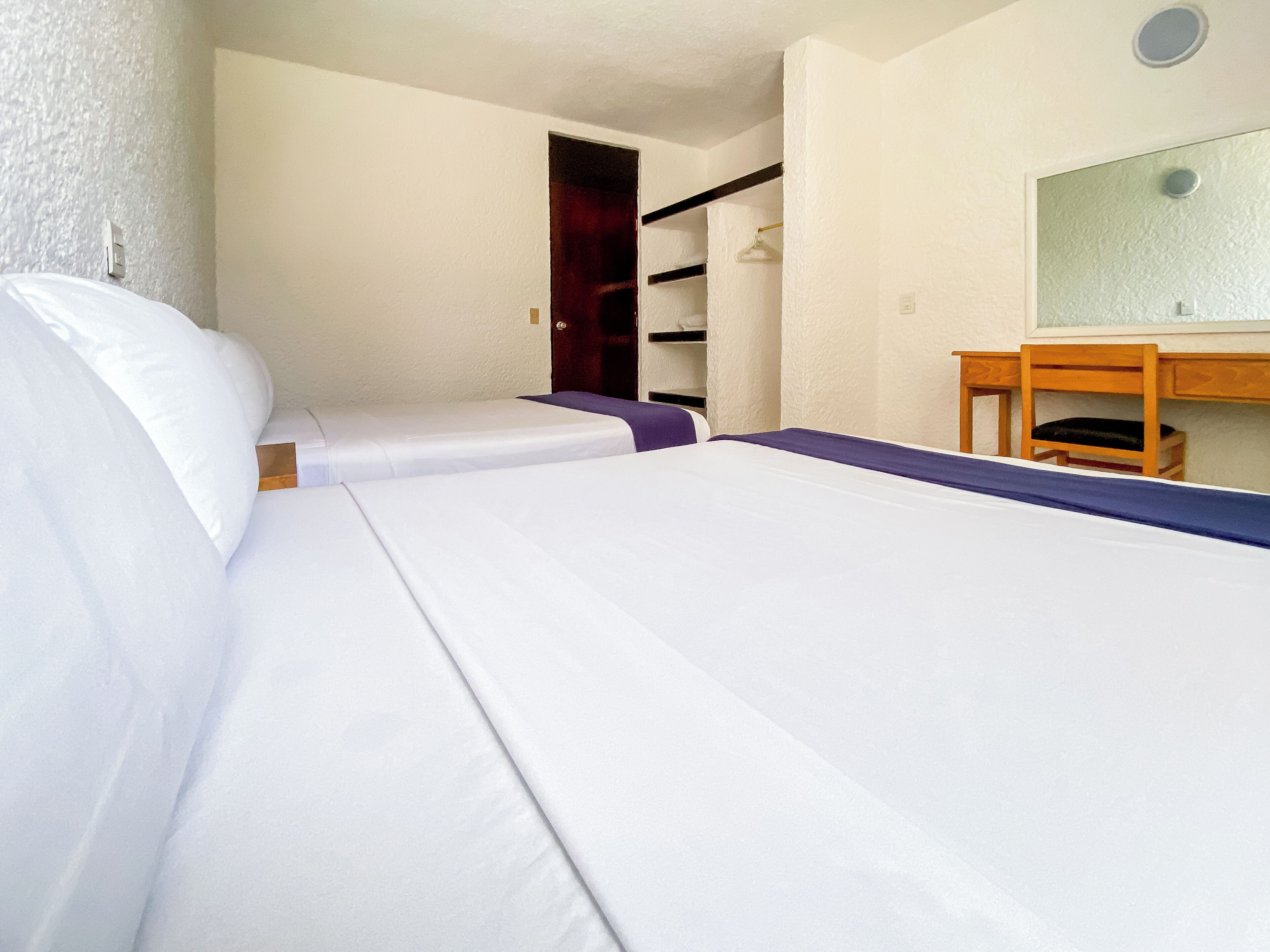 Quarto de hotel com cama, escrivaninha de madeira e guarda-roupa.