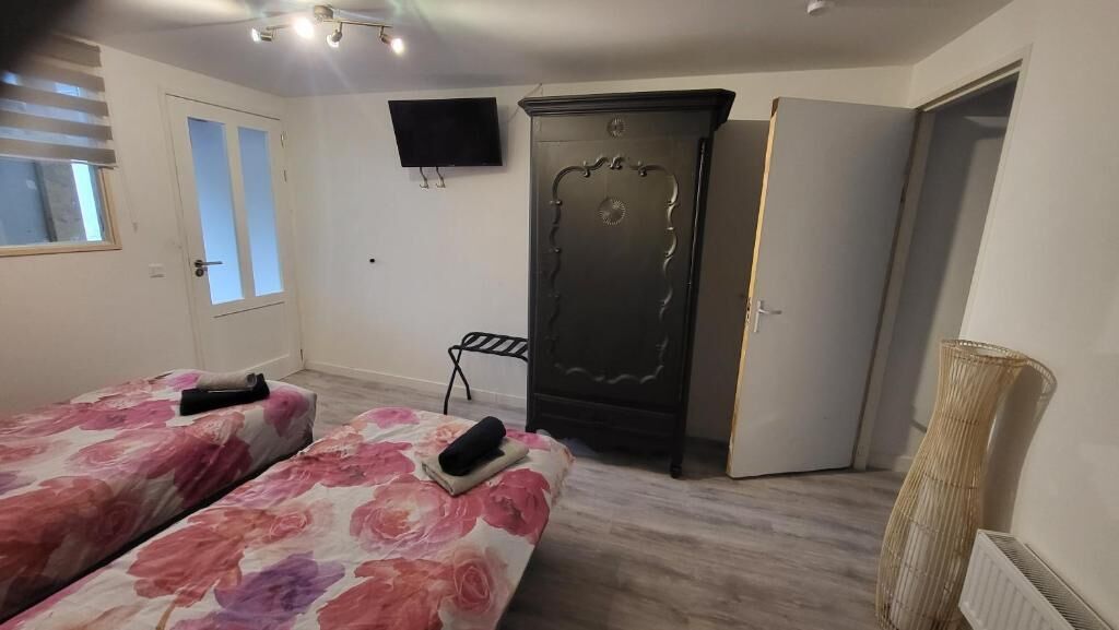 Quarto com duas camas, um guarda-roupa, uma televisão e uma janela.